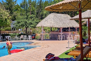 Área de piscina com espreguiçadeiras, bar e guarda-sóis de palha.