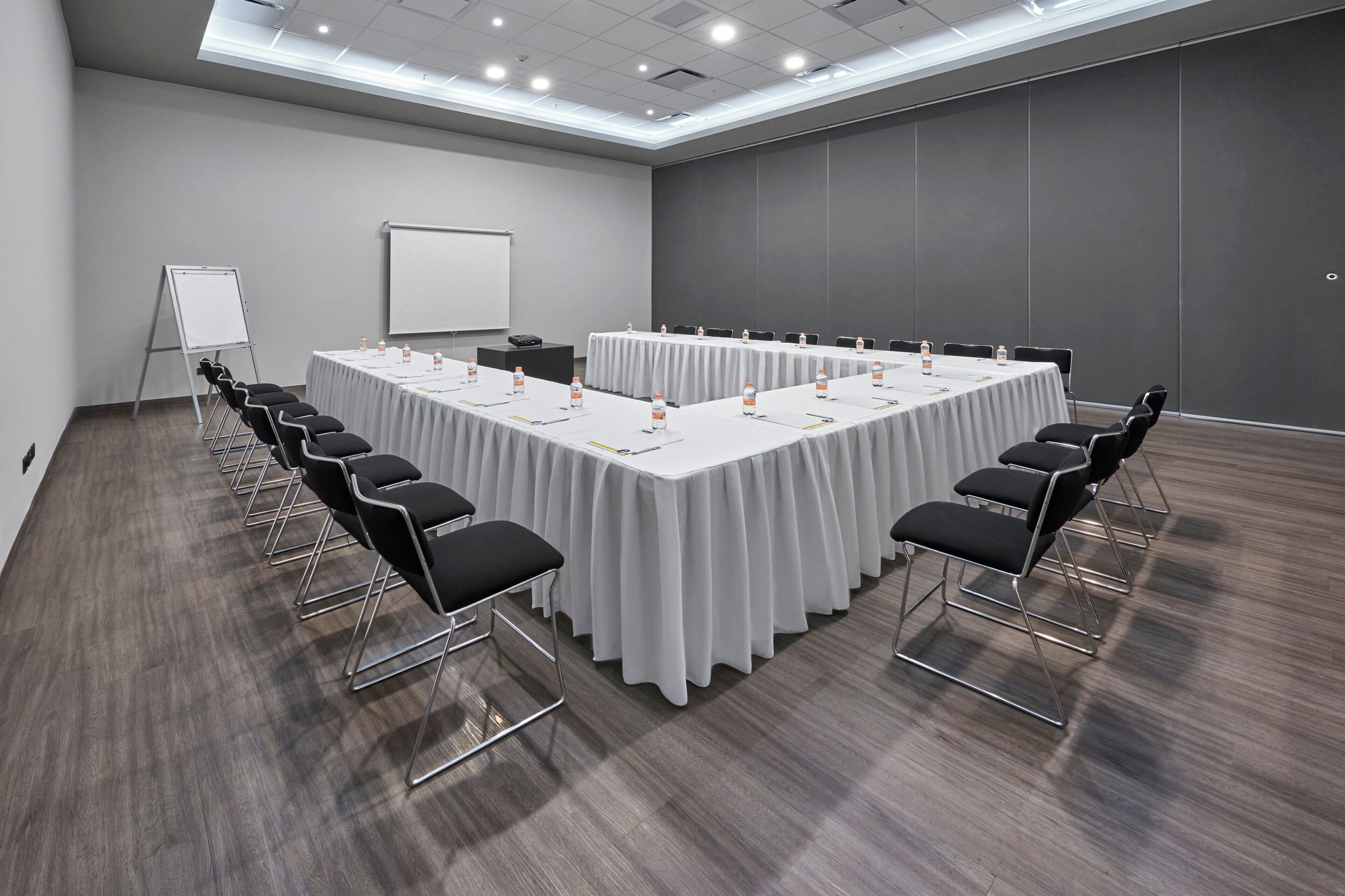 Uma sala de conferências com uma mesa comprida, cadeiras, um quadro branco e uma tela de projetor.