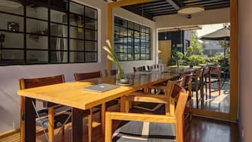 Uma sala de jantar ampla com uma longa mesa de madeira, várias cadeiras e grandes janelas que oferecem vista para o exterior.