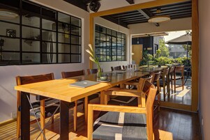 Uma sala de jantar ampla com uma longa mesa de madeira, várias cadeiras e grandes janelas que oferecem vista para o exterior.