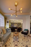 Uma sala de estar moderna com um piso estampado em padrão geométrico, um sofá, uma poltrona, uma mesa de centro redonda de madeira e um lustre de teto exclusivo.
