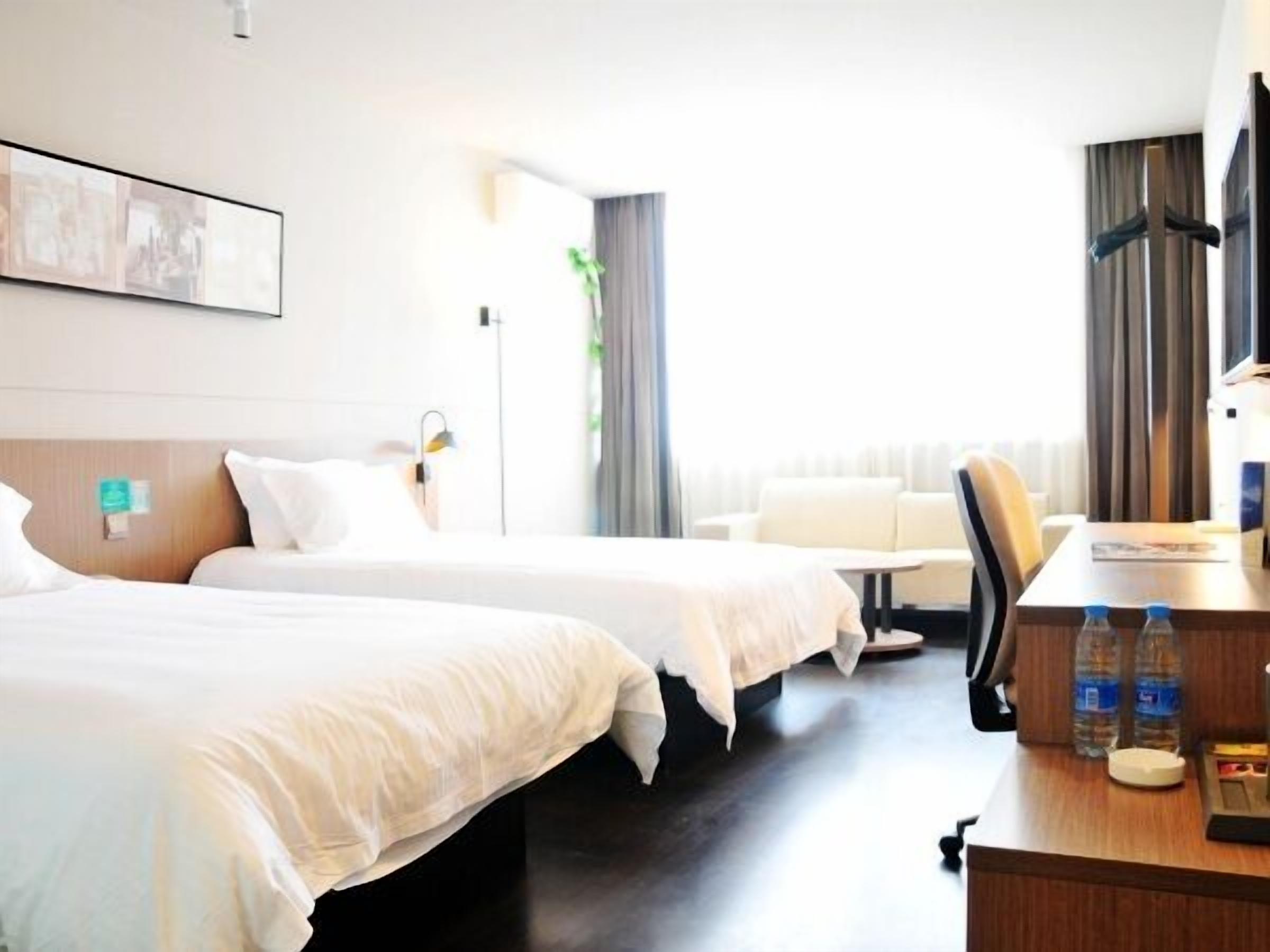Quarto de hotel com duas camas, uma escrivaninha com um computador e vista para a cidade.