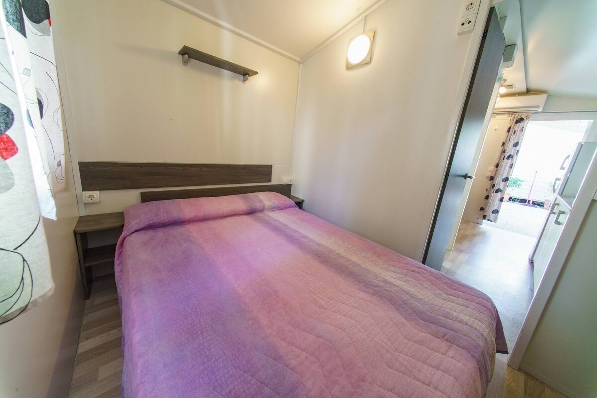 Um quarto pequeno e bem arrumado, com uma cama, uma mesa de cabeceira e um criado-mudo.