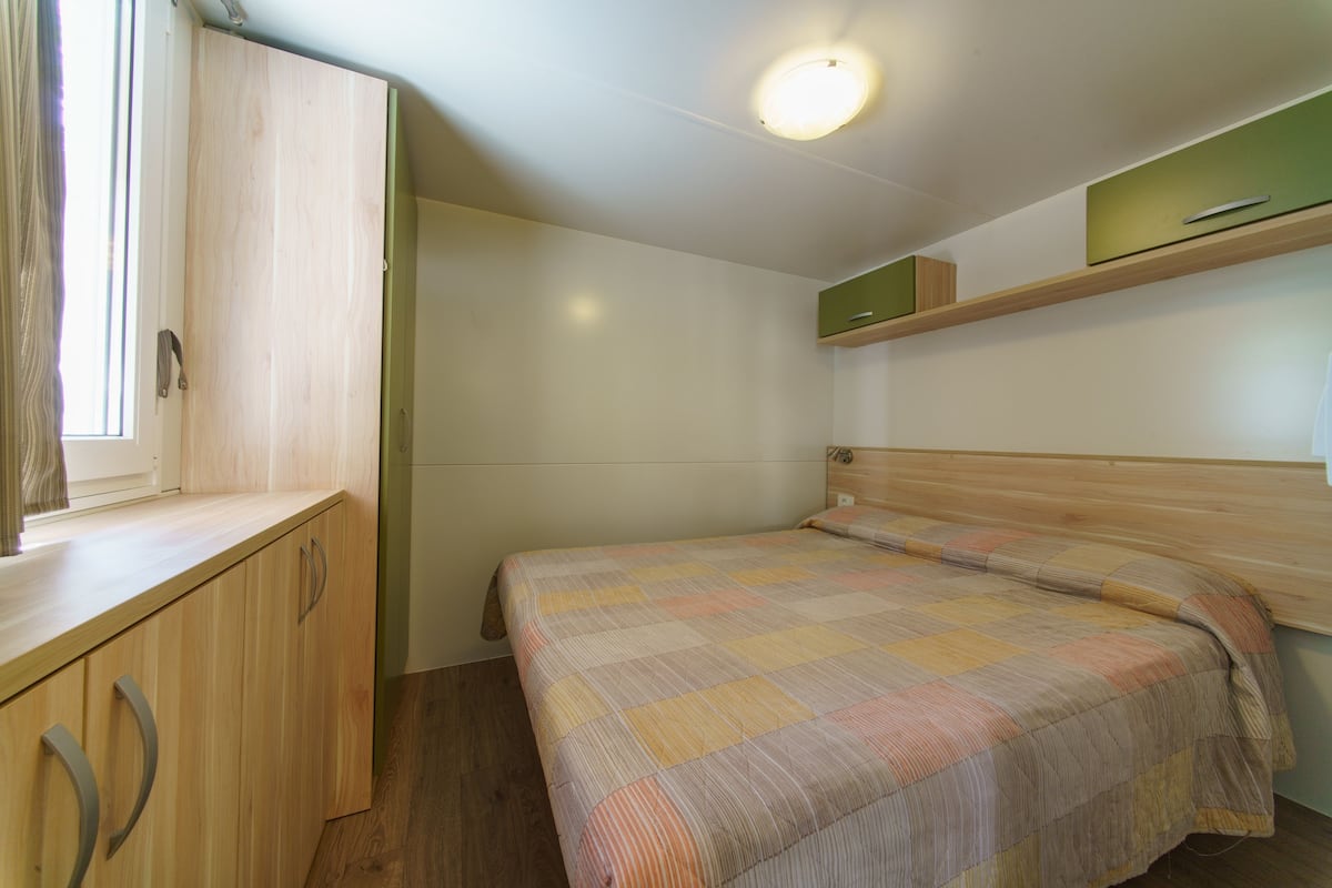 Quarto com cama, guarda-roupa de madeira e prateleira com uma caixa verde.