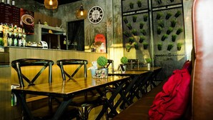 Um restaurante com mesa e cadeiras de madeira, um bar com garrafas e um relógio na parede.