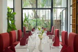 Mesa de jantar posta com cadeiras vermelhas estofadas, um vaso branco com uma flor e copos de vinho.