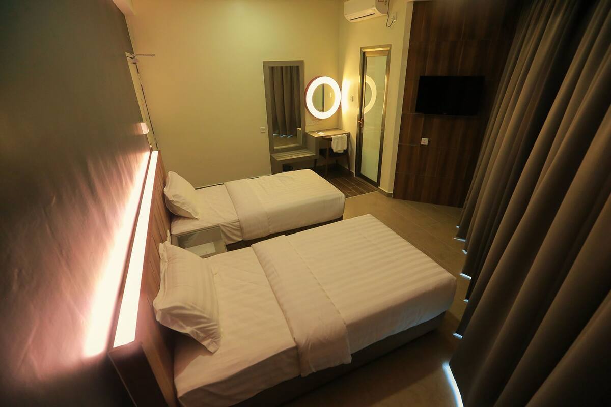 Quarto de hotel com duas camas, um espelho iluminado, televisão e uma porta.