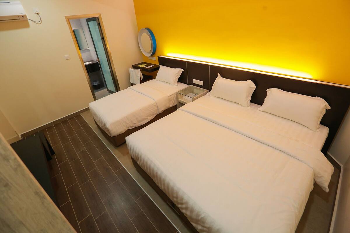 Quarto de hotel com duas camas, uma mesa de cabeceira com abajur, um espelho e um guarda-roupa.