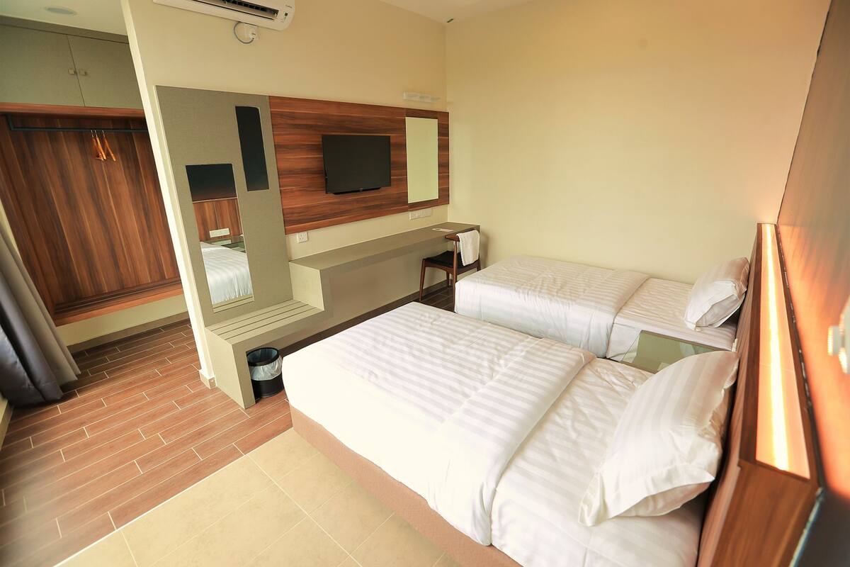 Quarto de hotel com duas camas, televisão, espelho e guarda-roupa de madeira.