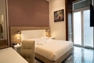 Quarto de hotel com cama, mesa de cabeceira, cadeira e obra de arte na parede.
