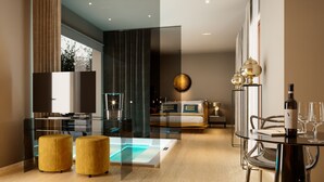 Quarto de hotel moderno com divisória de vidro, cama com cabeceira, mesa de cabeceira, abajur, garrafa de vinho e copos sobre uma mesa.