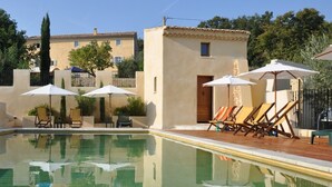 Uma área de piscina com espreguiçadeiras e guarda-sóis, rodeada por edifícios.