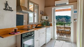 Cozinha com bancada de madeira, armários brancos, forno embutido e vista para uma varanda com mobiliário externo.