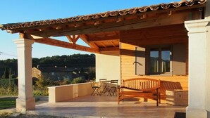Uma área de estar coberta ao ar livre com um banco de madeira, uma mesa e cadeiras.