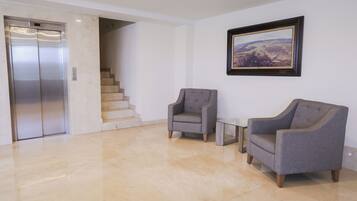 Um hall amplo com piso de mármore, uma escadaria, dois poltronas cinzas e um quadro de paisagem na parede.