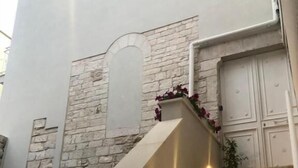 Uma escadaria com degraus de pedra e uma parede branca com detalhe em pedra e uma porta.