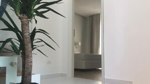 Interior moderno com uma planta em vaso, design minimalista e uma visão de um quarto com cama e cortinas.