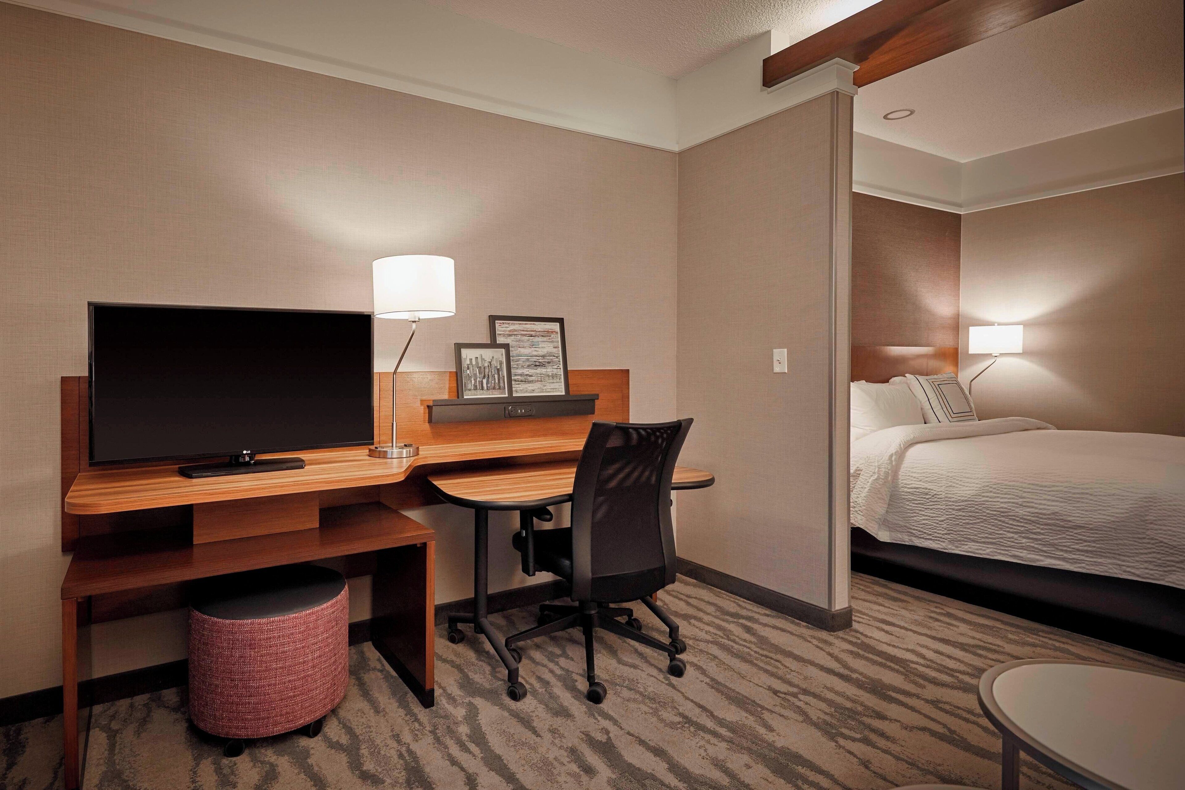 Quarto de hotel com televisão de tela plana, escrivaninha com cadeira, cama e uma mesa redonda pequena.