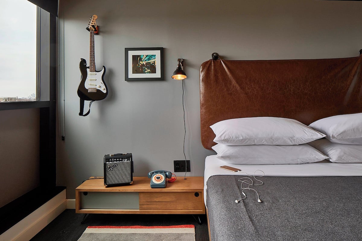Quarto com cama, almofadas, um violão, telefone e abajur.