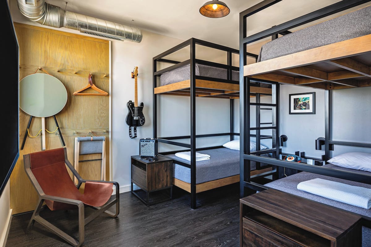 Quarto com beliche, uma cadeira de madeira, um violão e uma mesa pequena.