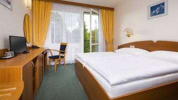 Quarto de hotel com cama, escrivaninha, cadeira e janela com cortinas.