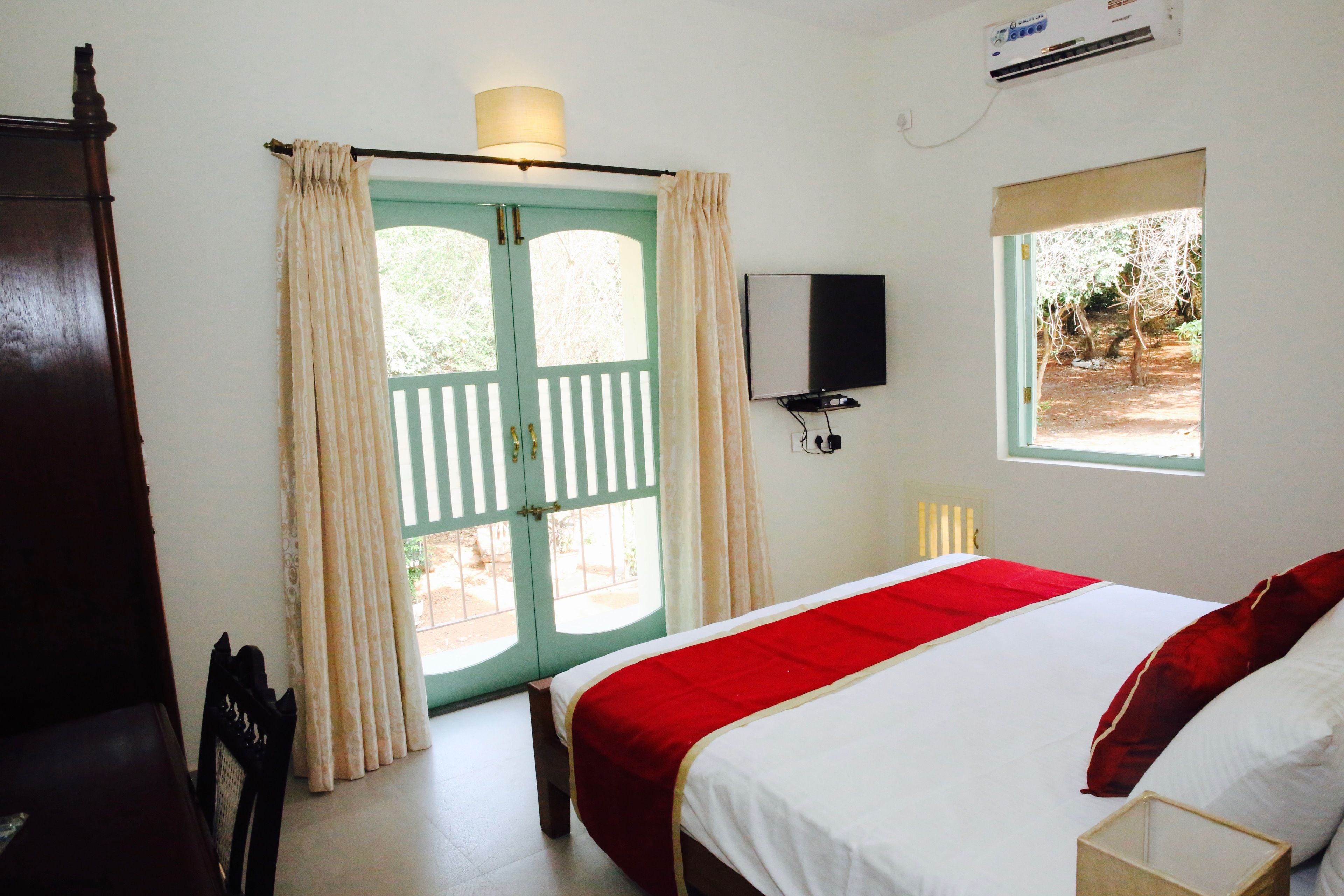 Um quarto com uma cama, televisão, janela e porta com cortinas.