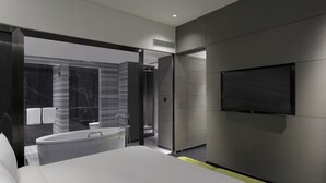 Quarto de hotel moderno com uma cama grande, banheira, chuveiro e televisão de tela plana na parede.