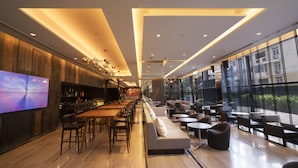 Um espaço de bar moderno com painéis de madeira, uma TV de tela plana e diversas opções de assento, incluindo mesas e sofás.
