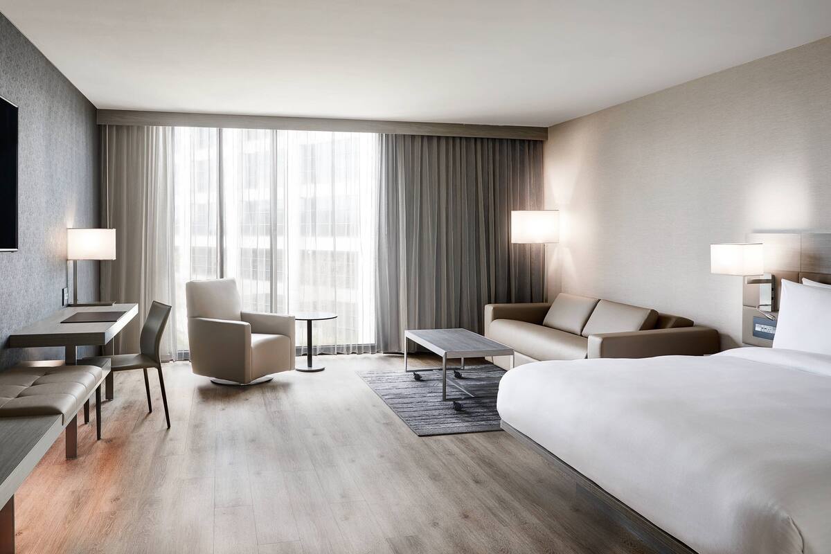 Quarto de hotel moderno com uma cama grande, um sofá, uma escrivaninha e uma cadeira.