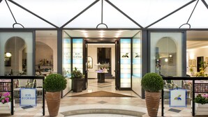 Entrada de hotel com design moderno, destacando fachada de vidro, área de recepção e escadaria que dá acesso ao interior.
