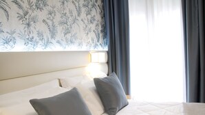 Quarto de hotel com cama, almofadas, cabeceira e janela com cortinas.