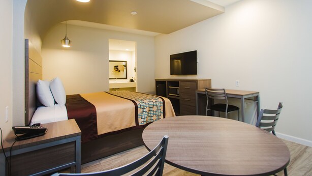Quarto de hotel com cama, mesa de cabeceira, escrivaninha, cadeira e televisão.