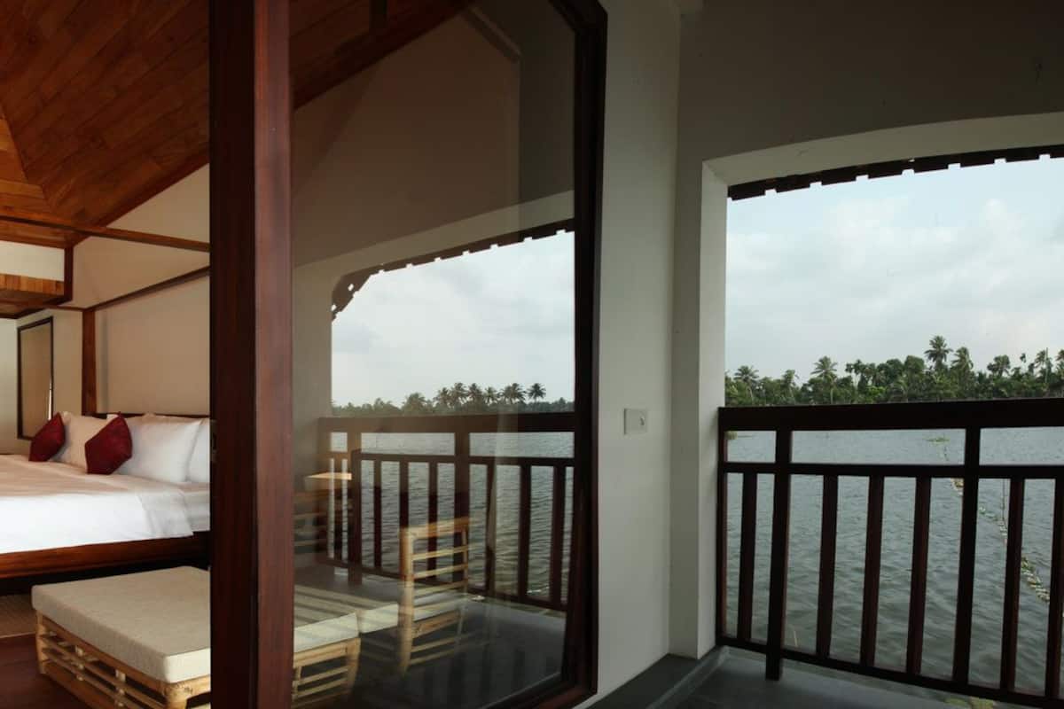 Quarto com teto de madeira, cama com manta vermelha e varanda com vista para a água.