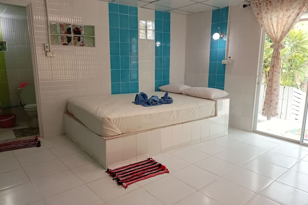 Um quarto com cama, janela com cortinas e um banheiro visível ao fundo.