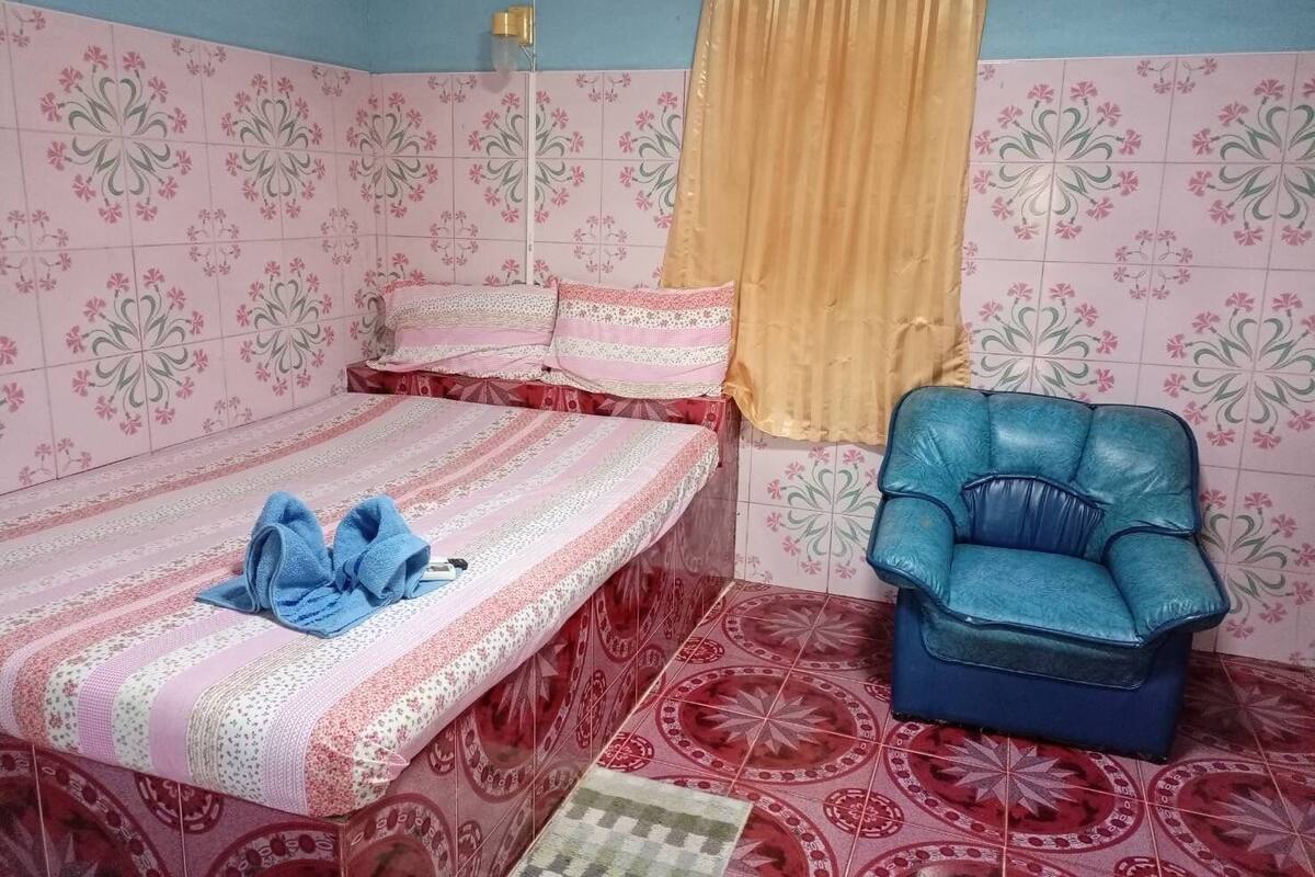 Quarto com uma cama, uma cadeira azul e paredes estampadas.