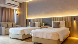 Quarto de hotel moderno com duas camas, um sofá, uma mesa de cabeceira e um aparelho de ar condicionado.