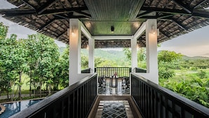Uma área externa coberta com piscina, espaço para sentar e vista para o verde ao redor.