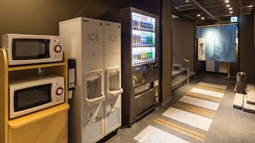 Máquina automática com distribuidor de bebidas e micro-ondas numa prateleira.