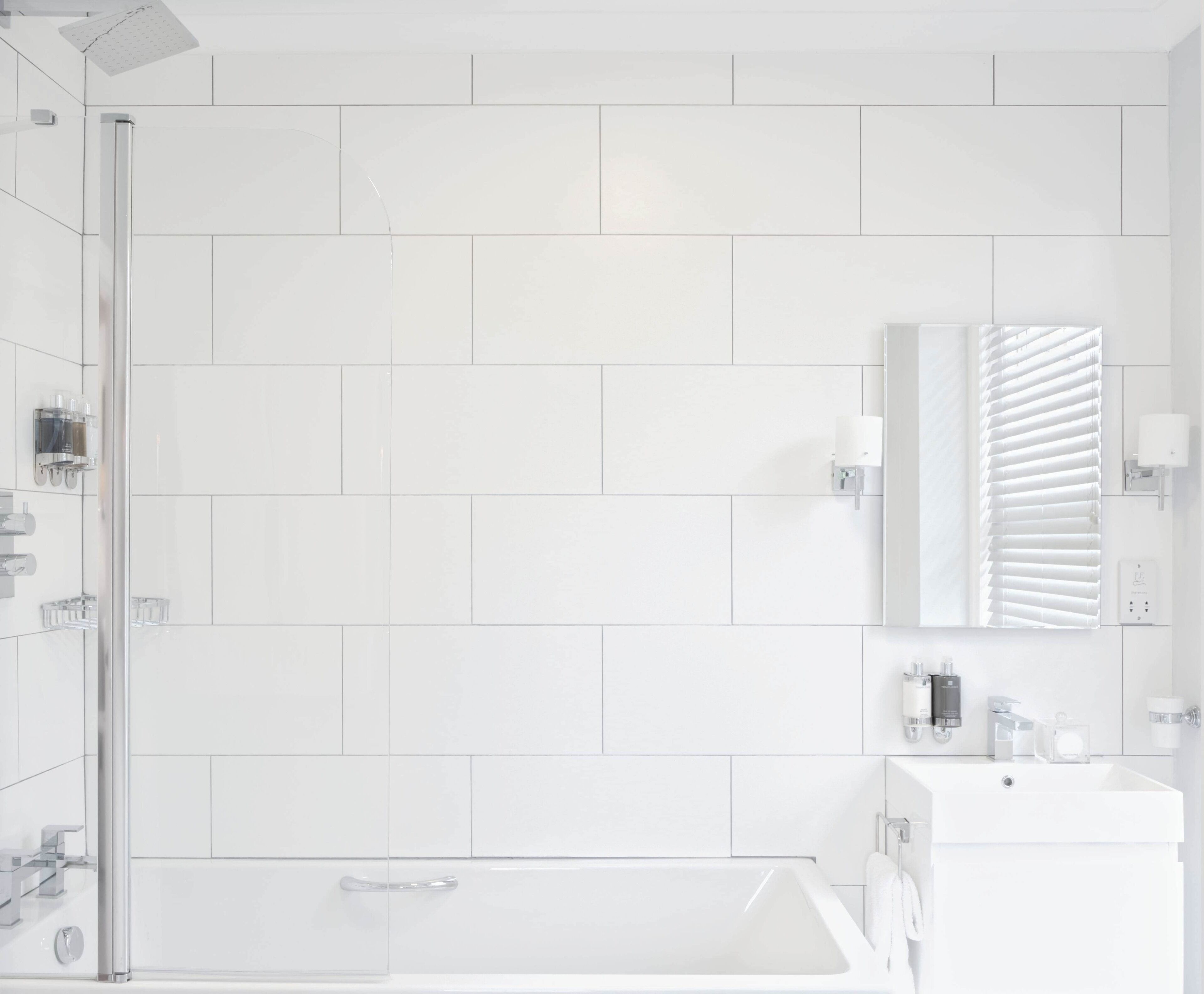 Casa de banho moderna com azulejos brancos, cabine de duche em vidro, lavatório branco e espelho com porta-toalhas.