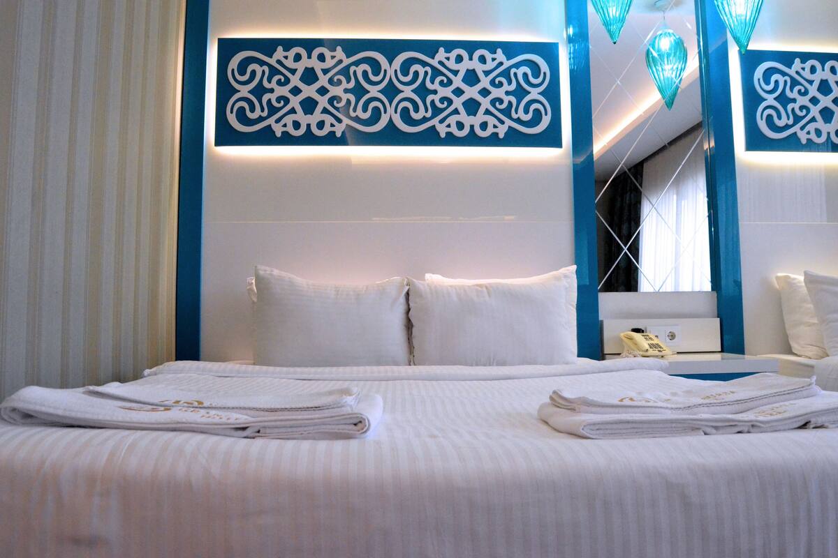 Quarto de hotel com cama bem arrumada, telefone de mesa e painéis decorativos na parede.