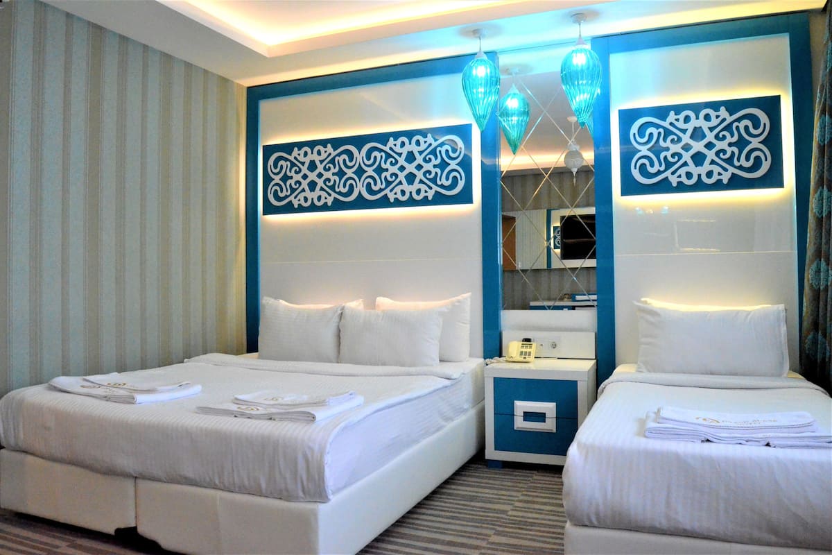 Quarto de hotel com duas camas, uma mesa de cabeceira e painéis decorativos na parede.