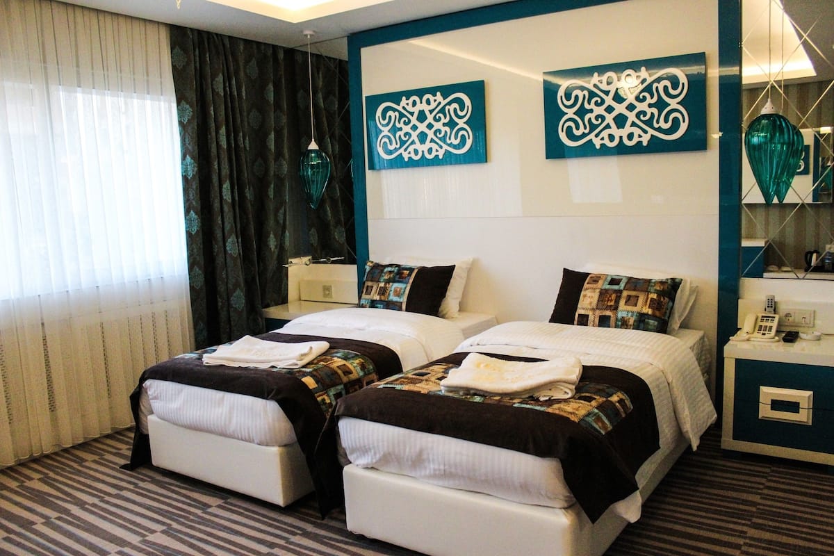Quarto de hotel com duas camas, uma mesa de cabeceira e um objeto decorativo na parede.