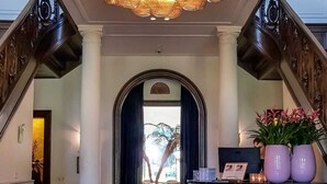 Um hall imponente com um candelabro, uma mesa de recepção e uma escadaria.