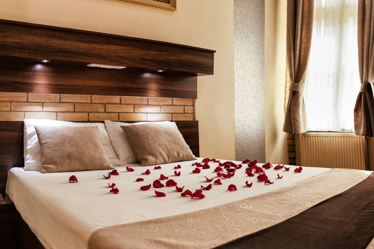 Quarto de hotel com uma cama grande, cabeceira com padrão de tijolos, quadro na parede e janela com cortinas.