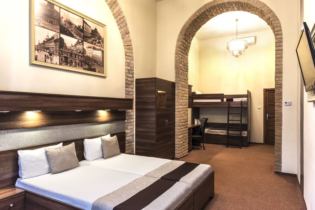 Quarto de hotel com uma cama grande, uma escrivaninha e beliches.