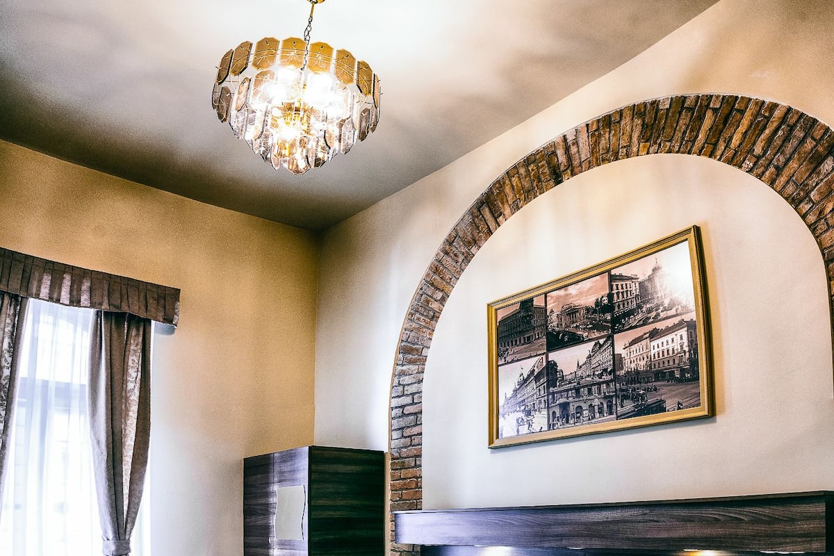 Um quarto amplo com uma cama grande, um candelabro, um arco de tijolos e uma pintura da paisagem urbana.