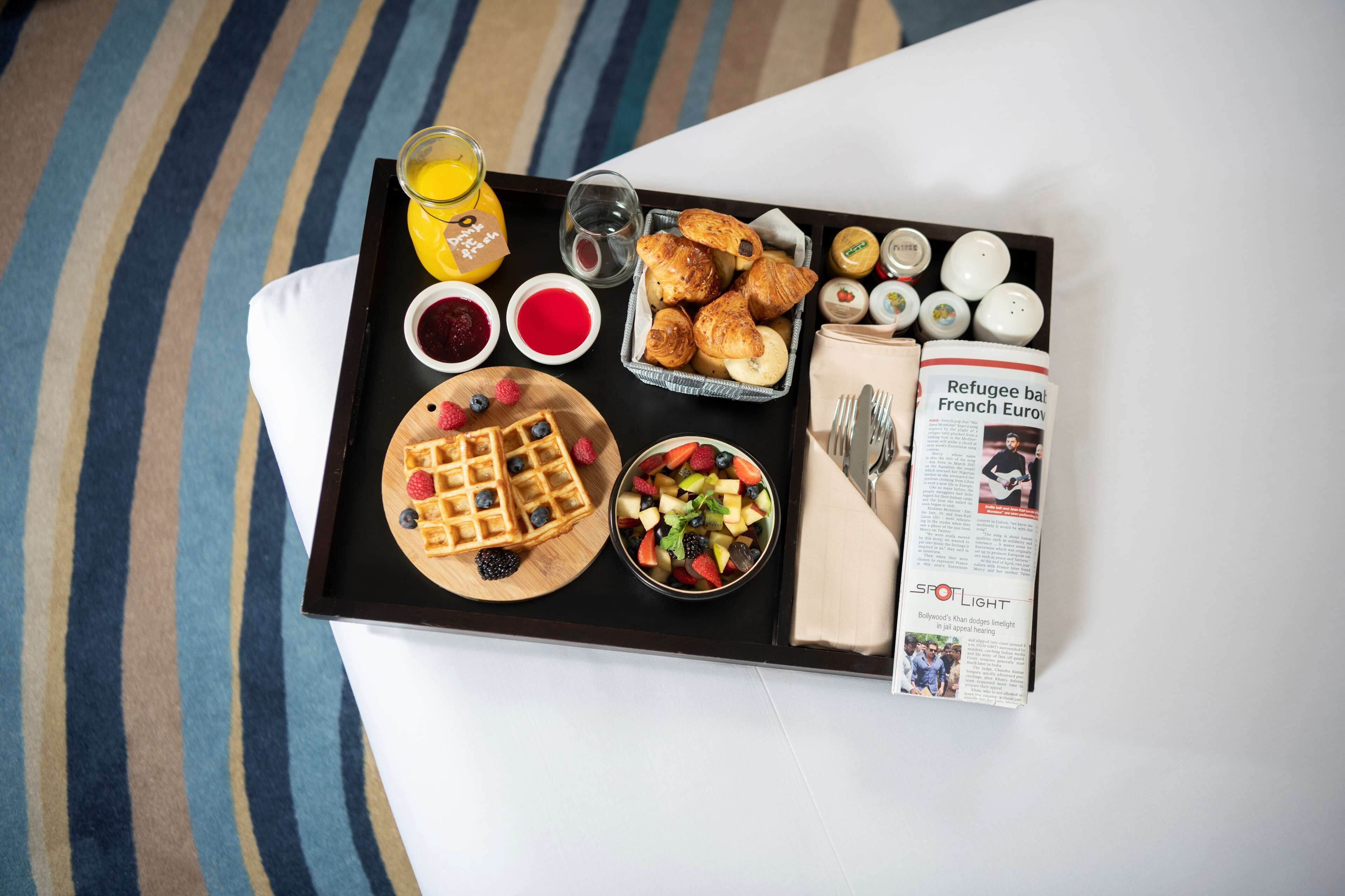 Bandeja de café da manhã com waffles, frutas, croissants e um jornal.
