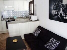 Espaço compacto com cozinha compacta, um sofá preto com almofadas estampadas e uma pequena mesa com um sanduíche.