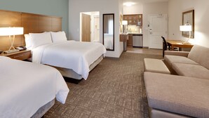 Quarto de hotel com duas camas, área de estar, cozinha compacta e banheiro.