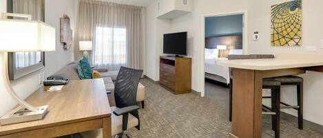 Quarto de hotel com escrivaninha, cadeira de escritório, cama, TV e obras de arte.